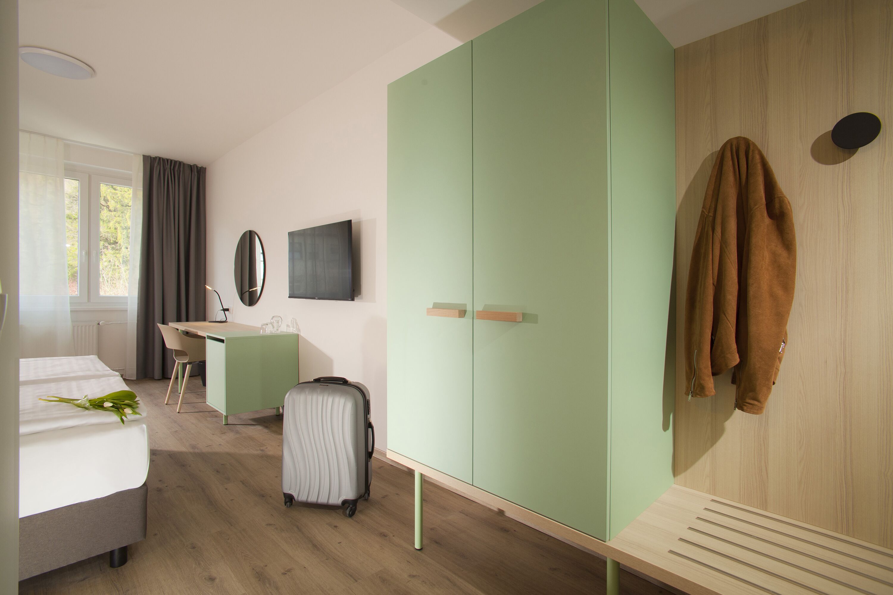Quarto de hotel moderno com cama, escrivaninha, guarda-roupa e mala.