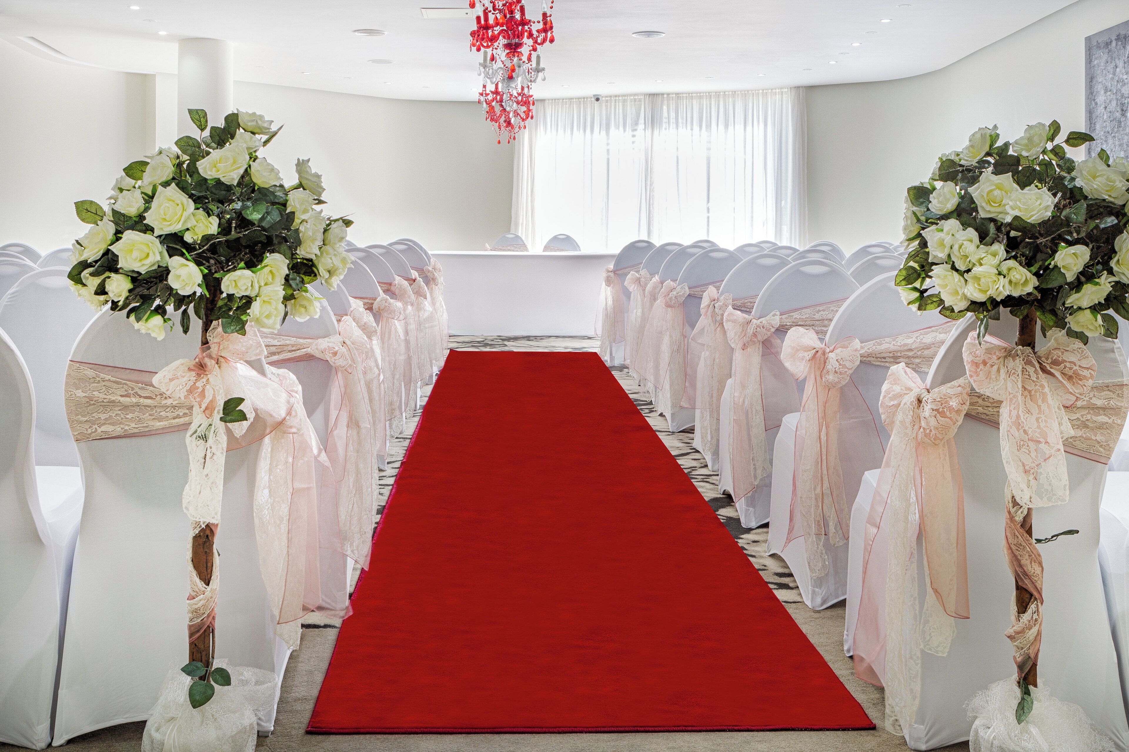 Capela de hotel com cadeiras brancas, tapete vermelho e decoração floral.