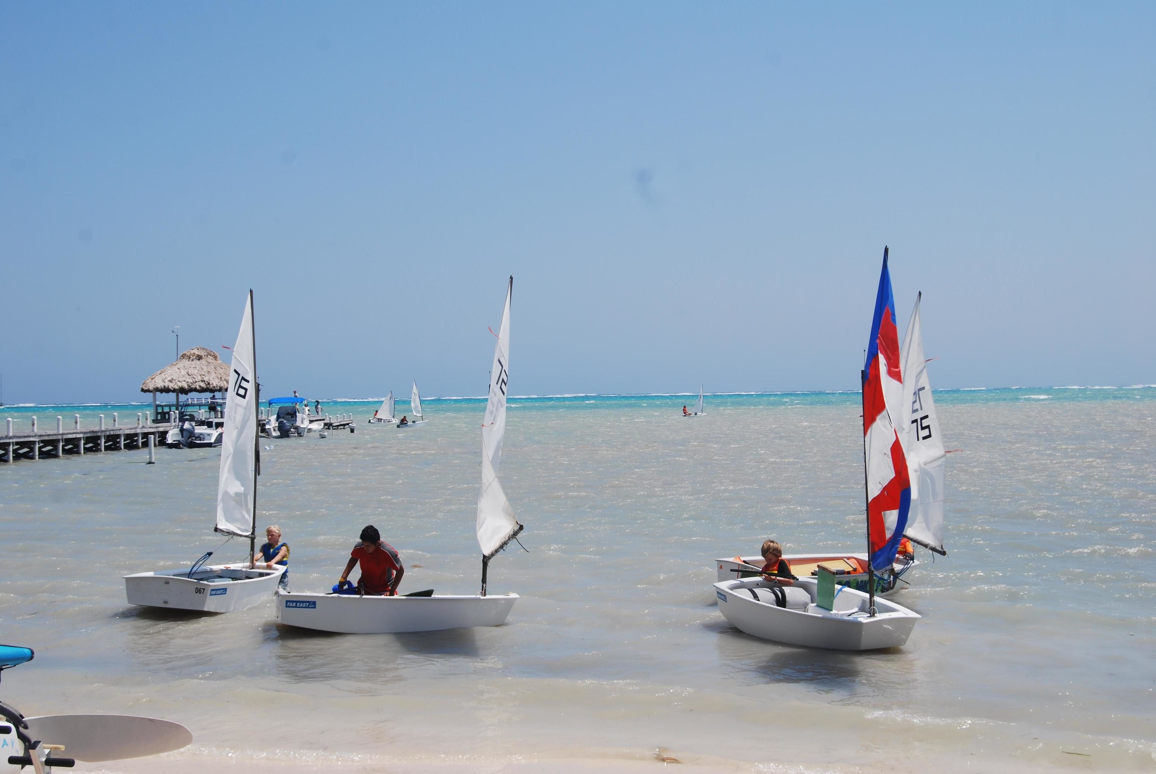 Três barcos à vela em uma praia calma, com céu claro.