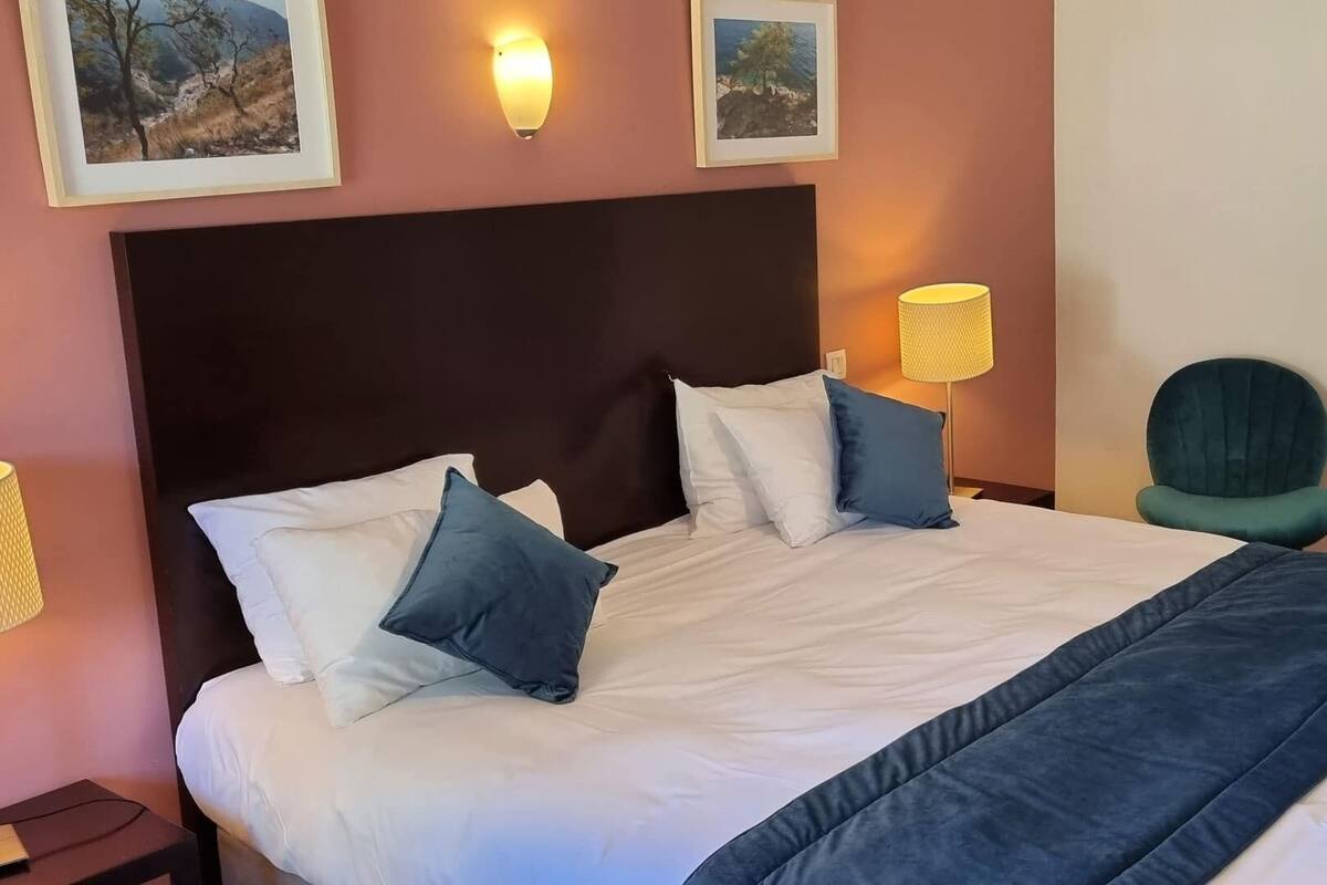 Cama bem arrumada com almofadas brancas e azuis, cabeceira escura e quadros na parede.