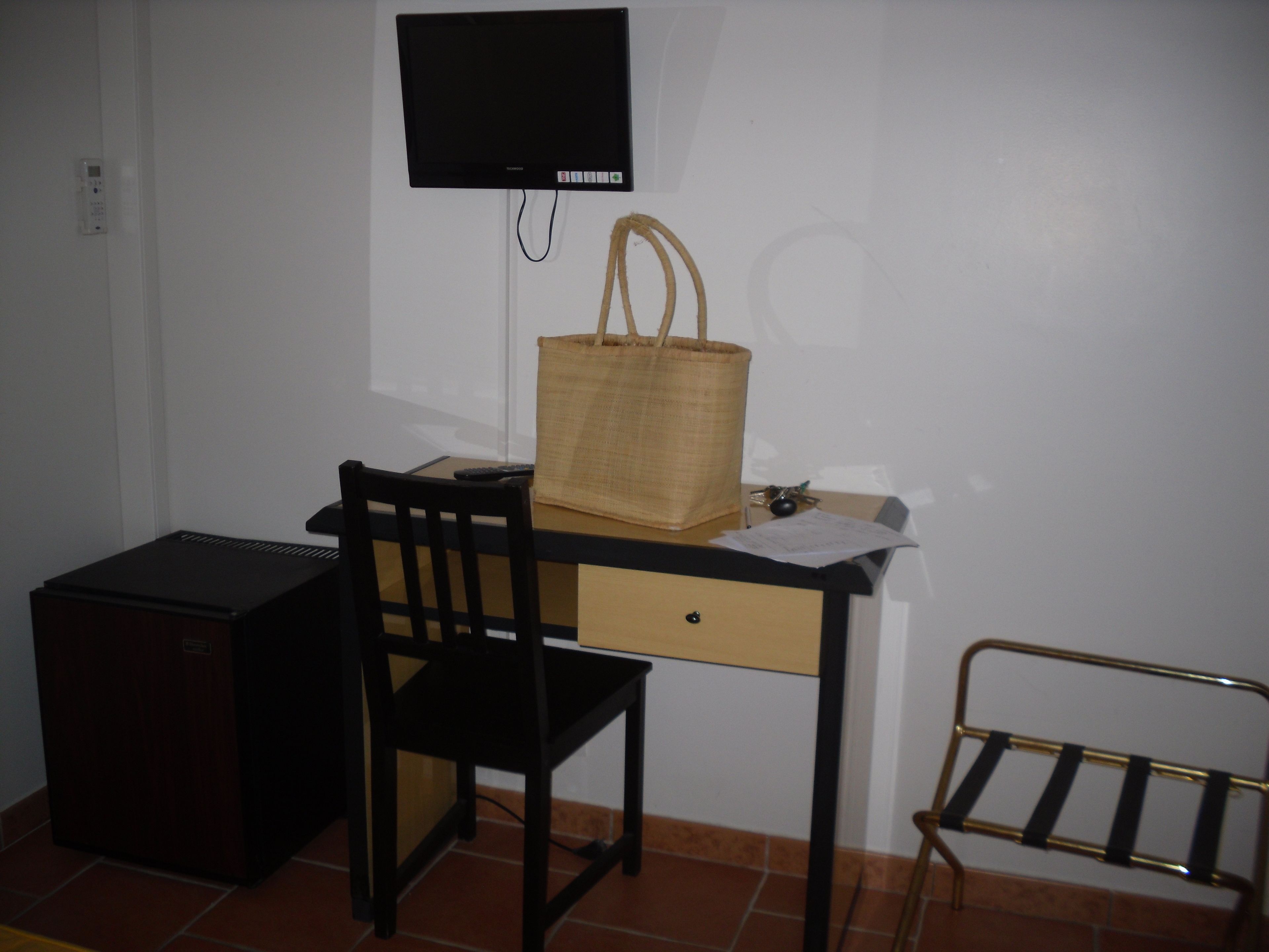 Um quarto pequeno com uma escrivaninha, cadeira e televisão fixada na parede.