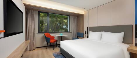 Quarto de hotel moderno com uma cama grande, uma escrivaninha, uma cadeira, uma televisão e uma janela com cortinas.