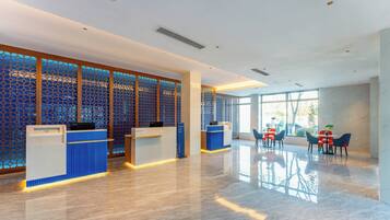 Um lobby de hotel moderno, com dois balcões de recepção, uma área de estar com cadeiras e uma parede decorativa com padrão azul.
