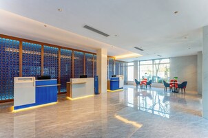 Um lobby de hotel moderno, com dois balcões de recepção, uma área de estar com cadeiras e uma parede decorativa com padrão azul.