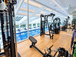 Academia com equipamentos de ginástica, um banco e vista para uma piscina ao ar livre.