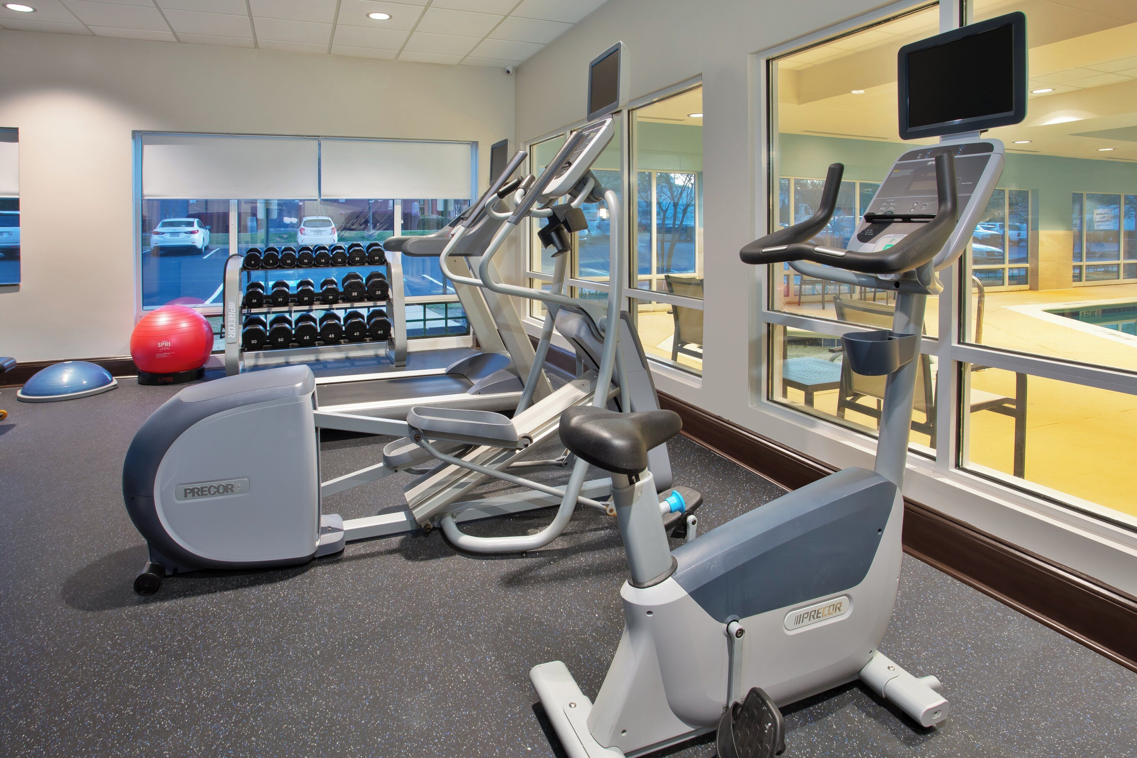Academia com esteiras, elíptica e uma bola de exercícios vermelha.
