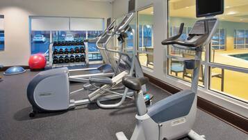 Academia com esteiras, elíptica e uma bola de exercícios vermelha.