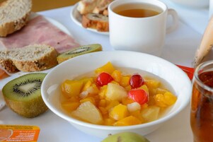 Mesa de café da manhã com uma tigela de frutas, fatias de pão, uma xícara de chá e um copo de suco.