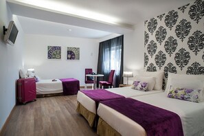 Quarto de hotel com duas camas, uma escrivaninha, uma cadeira e uma televisão.