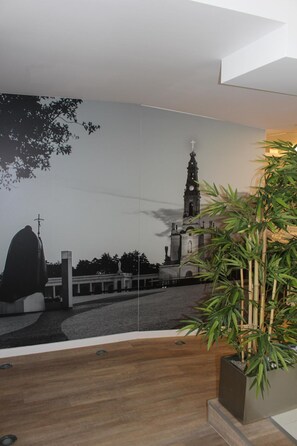 Quarto com um grande mural de uma igreja e uma cruz, piso de madeira e uma planta de bambu em um vaso.