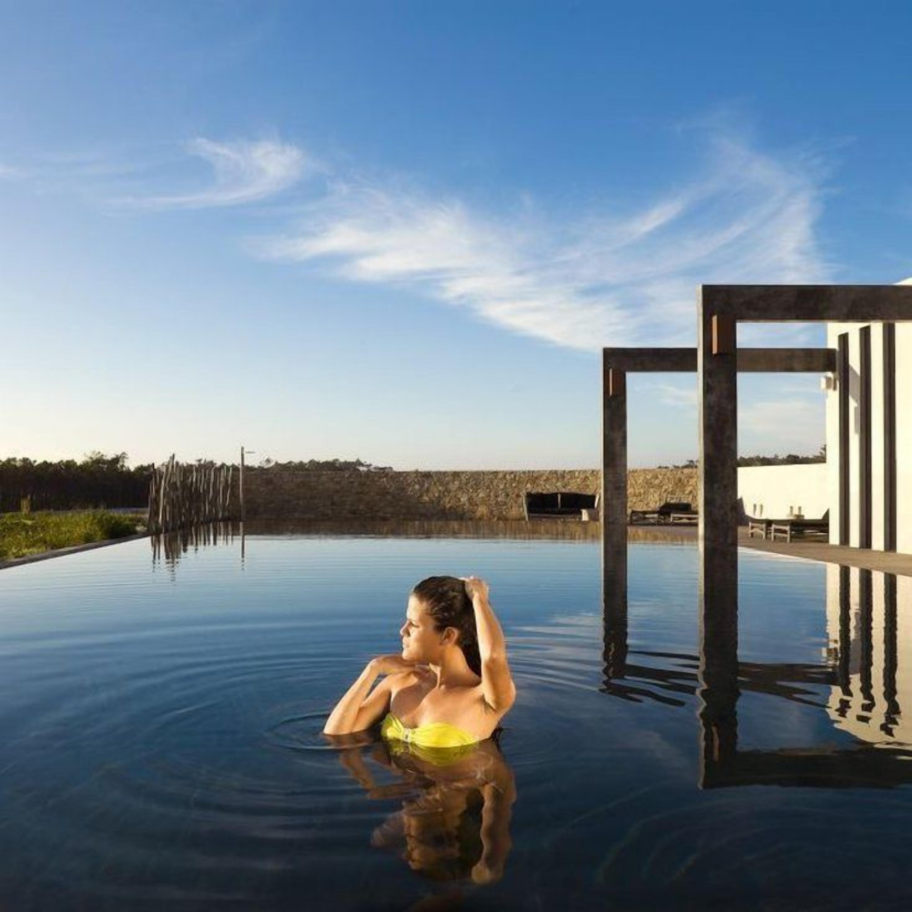 Uma pessoa em uma piscina transparente com uma estrutura de madeira à direita.