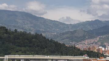 Uma estação de trem com um trem nos trilhos, cercada por colinas e um horizonte urbano ao fundo.