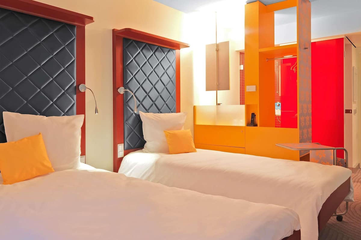 Quarto de hotel com duas camas, uma porta vermelha e um espelho.