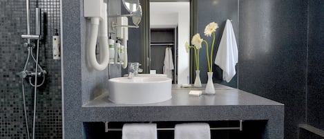 Um banheiro moderno com um espelho grande, pia e chuveiro. Toalhas penduradas em um porta-toalhas e um vaso com flores no balcão.