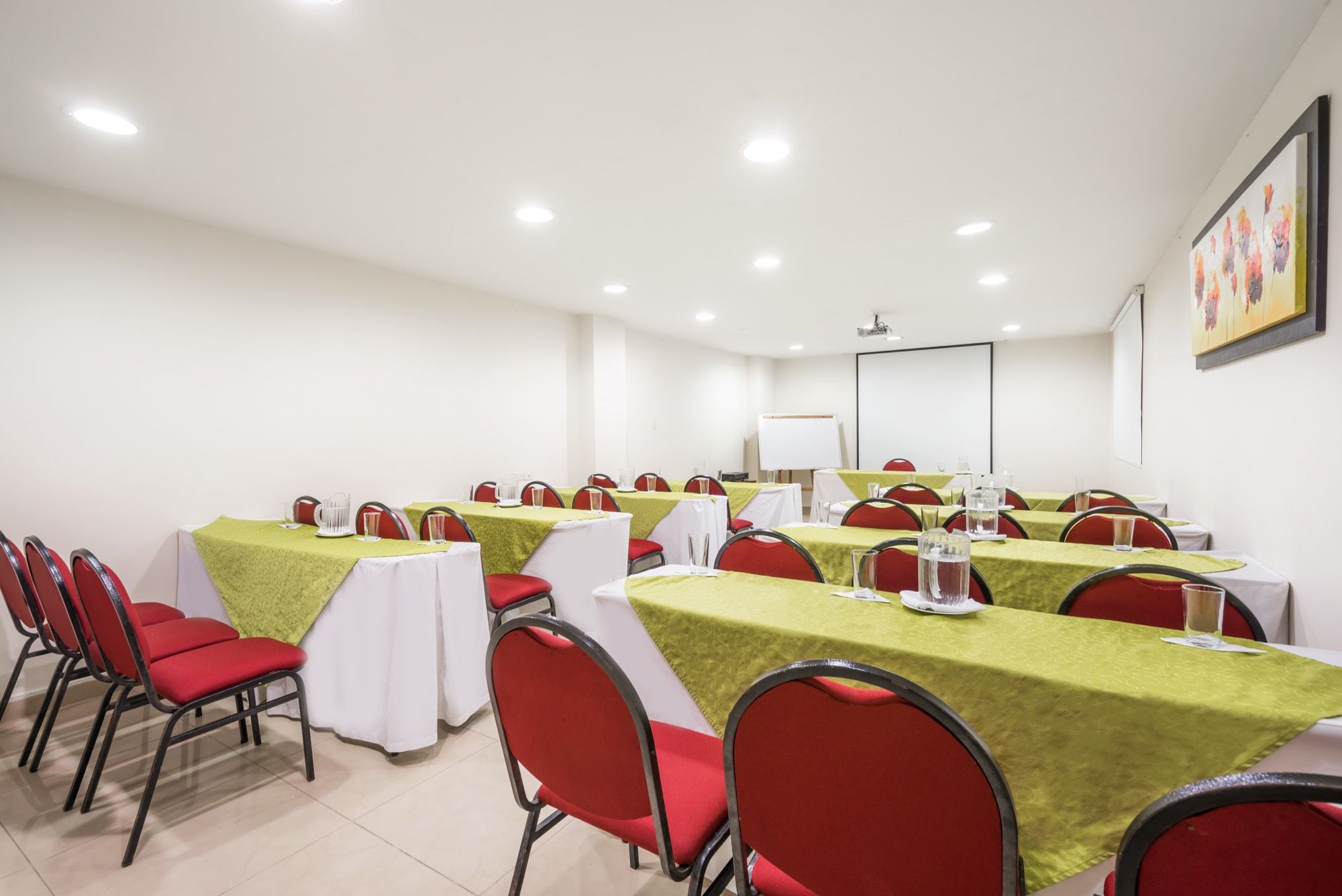 Sala de conferência com várias mesas, cadeiras vermelhas e um quadro branco.