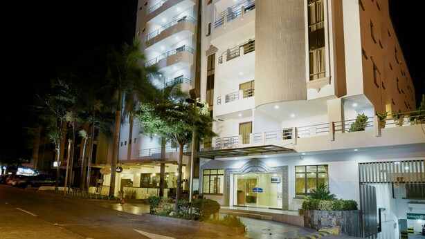 Um hotel com vários andares, um letreiro chamativo com a palavra 'HOTEL', fachada moderna e entrada bem iluminada.