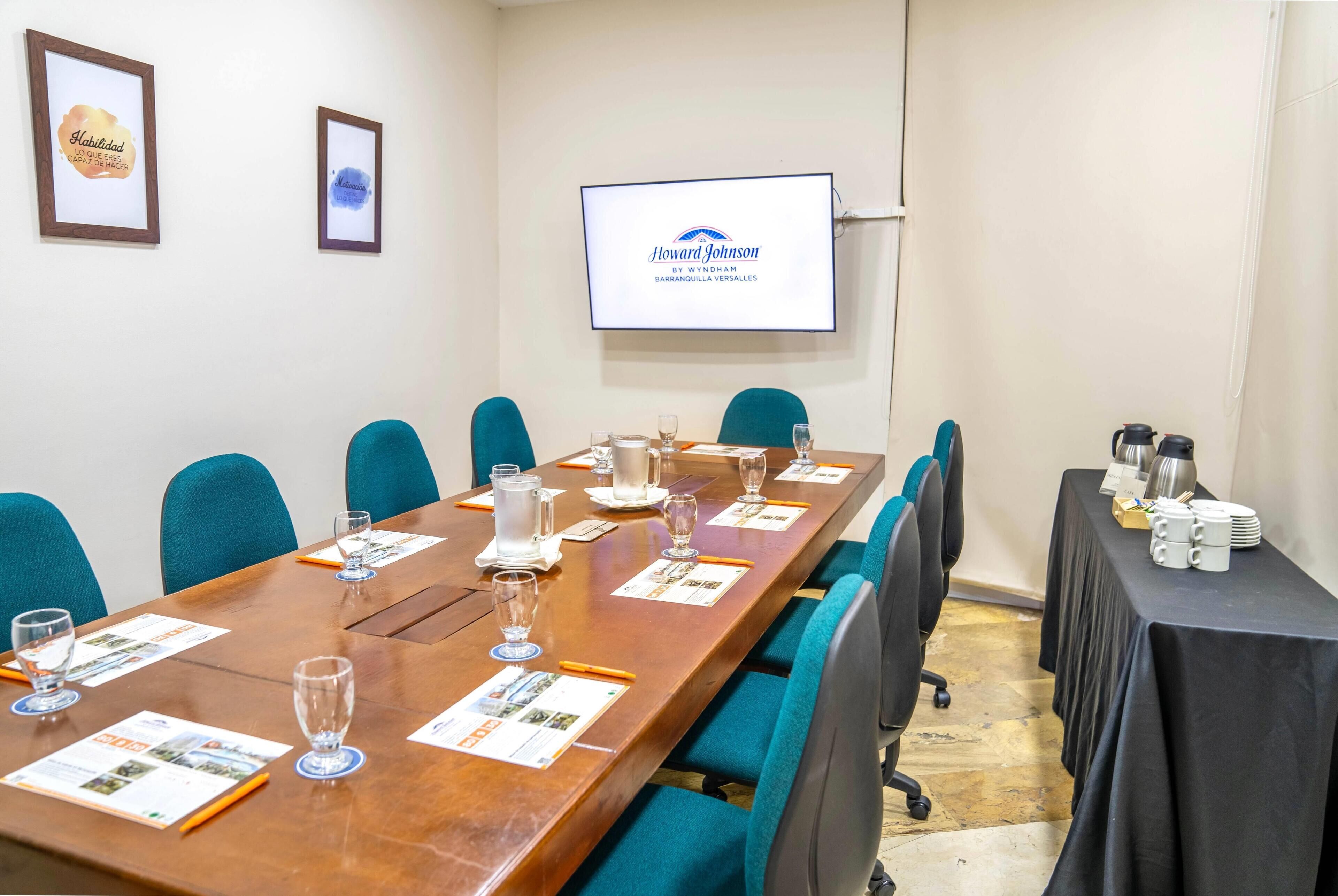 Sala de conferências com uma mesa grande, cadeiras e uma tela exibindo um logotipo.