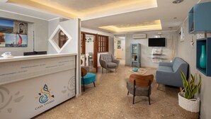 Um saguão de hotel com balcão de recepção, área de estar, televisão e obras de arte.