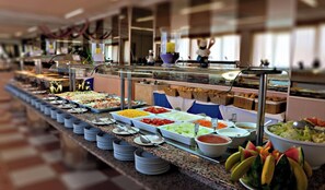 Buffet com diversas estações de comida, incluindo saladas, frutas e sobremesas.