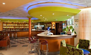 Uma área de bar com banquetas, balcão e prateleiras com garrafas.