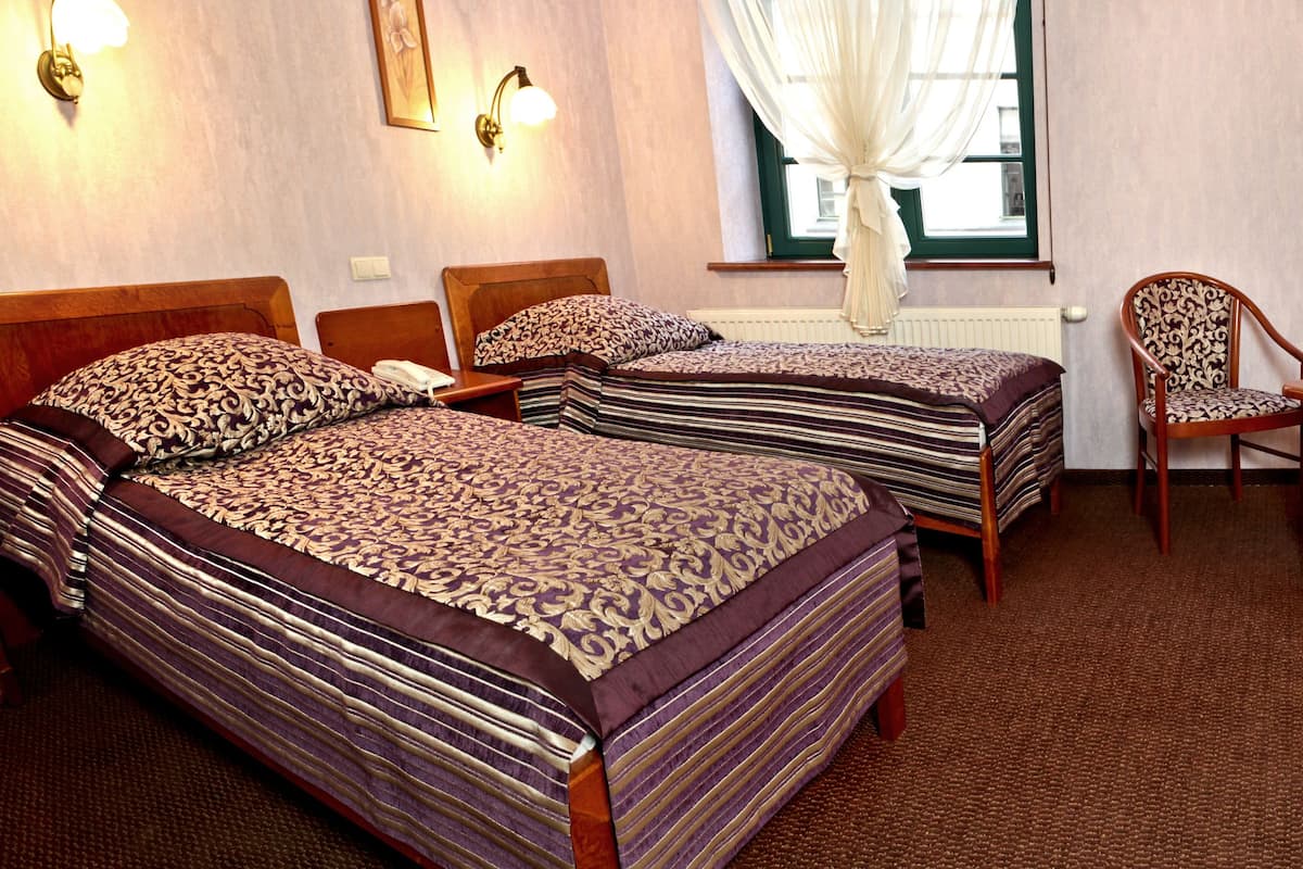 Quarto de hotel com duas camas, uma escrivaninha, uma cadeira, uma televisão e uma janela com cortinas.