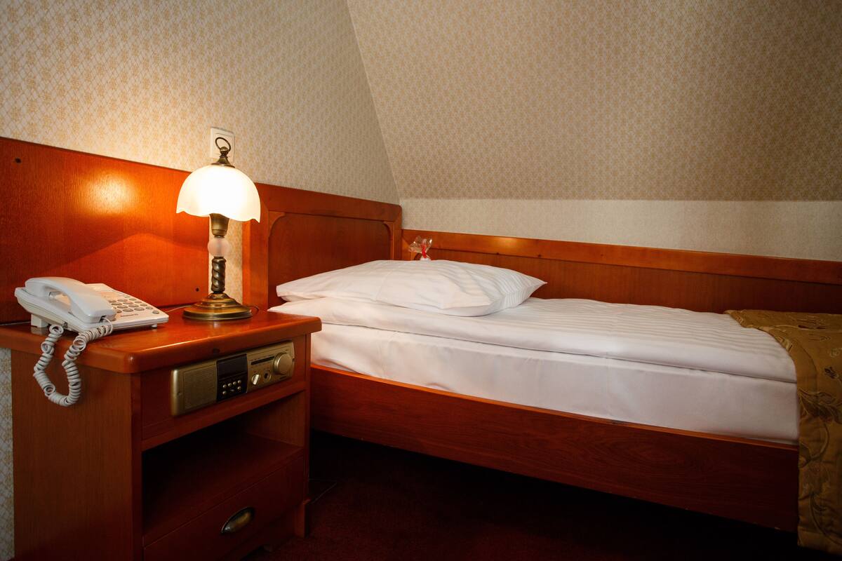 Quarto de hotel com cabeceira de madeira, cama com roupa de cama branca, luminária de cabeceira, telefone e mesa de cabeceira pequena.