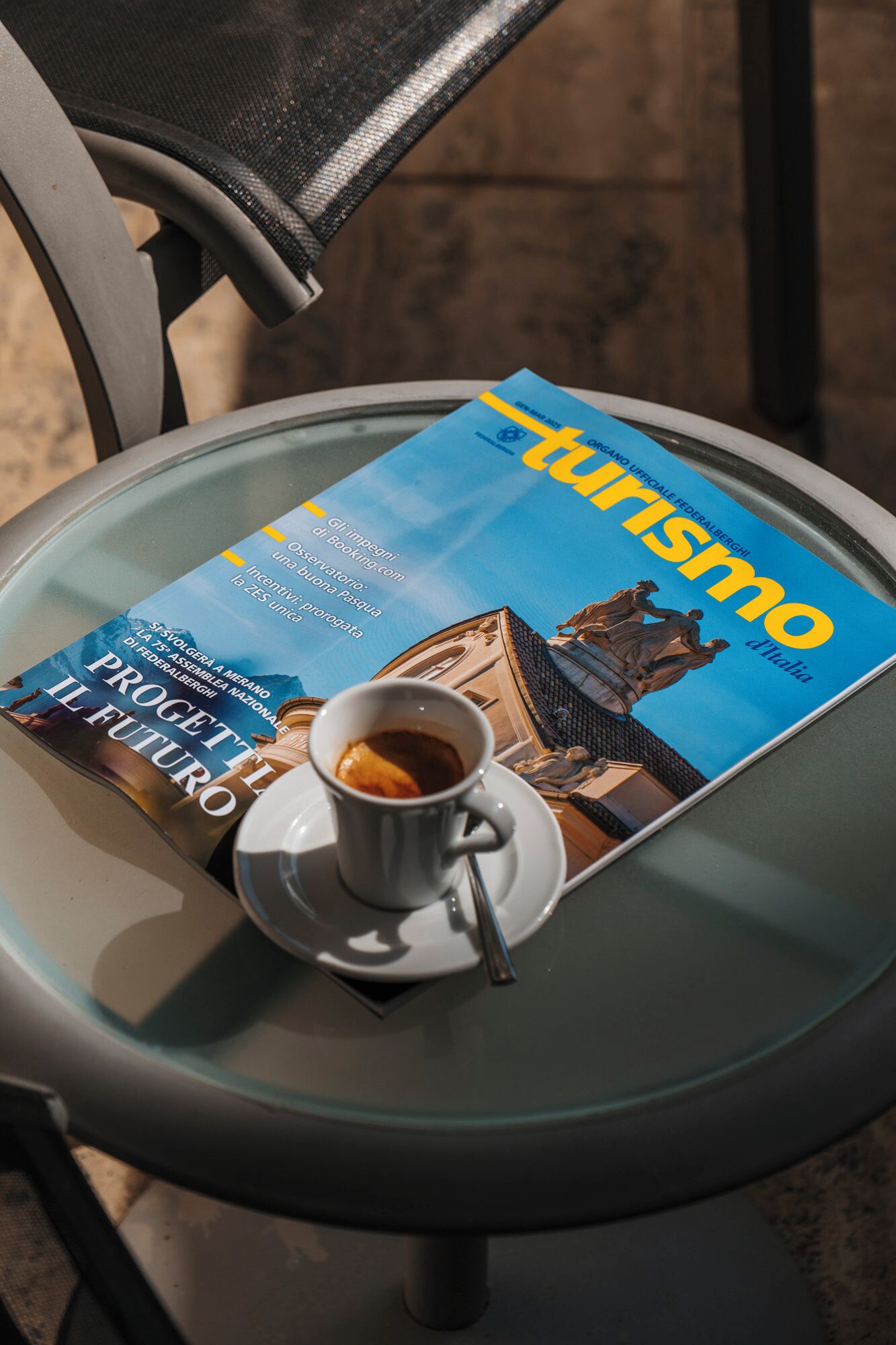 Uma mesa de vidro com uma revista, uma chávena de café e uma colher.