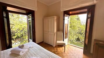 Quarto com cama, cadeira, guarda-roupa e varanda com vista para árvores.