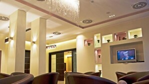 Um saguão de hotel moderno com área de estar, uma tela de televisão e prateleiras decorativas na parede.