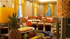 Uma sala de jantar de hotel com mesas preparadas para o pequeno-almoço, exibindo uma variedade de frutas e bebidas.