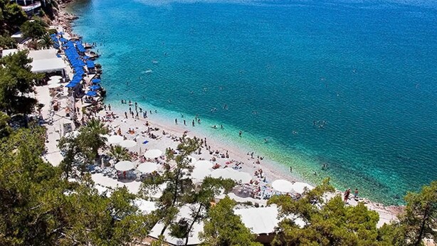 Uma praia com águas azul-claras, guarda-sóis e pessoas.