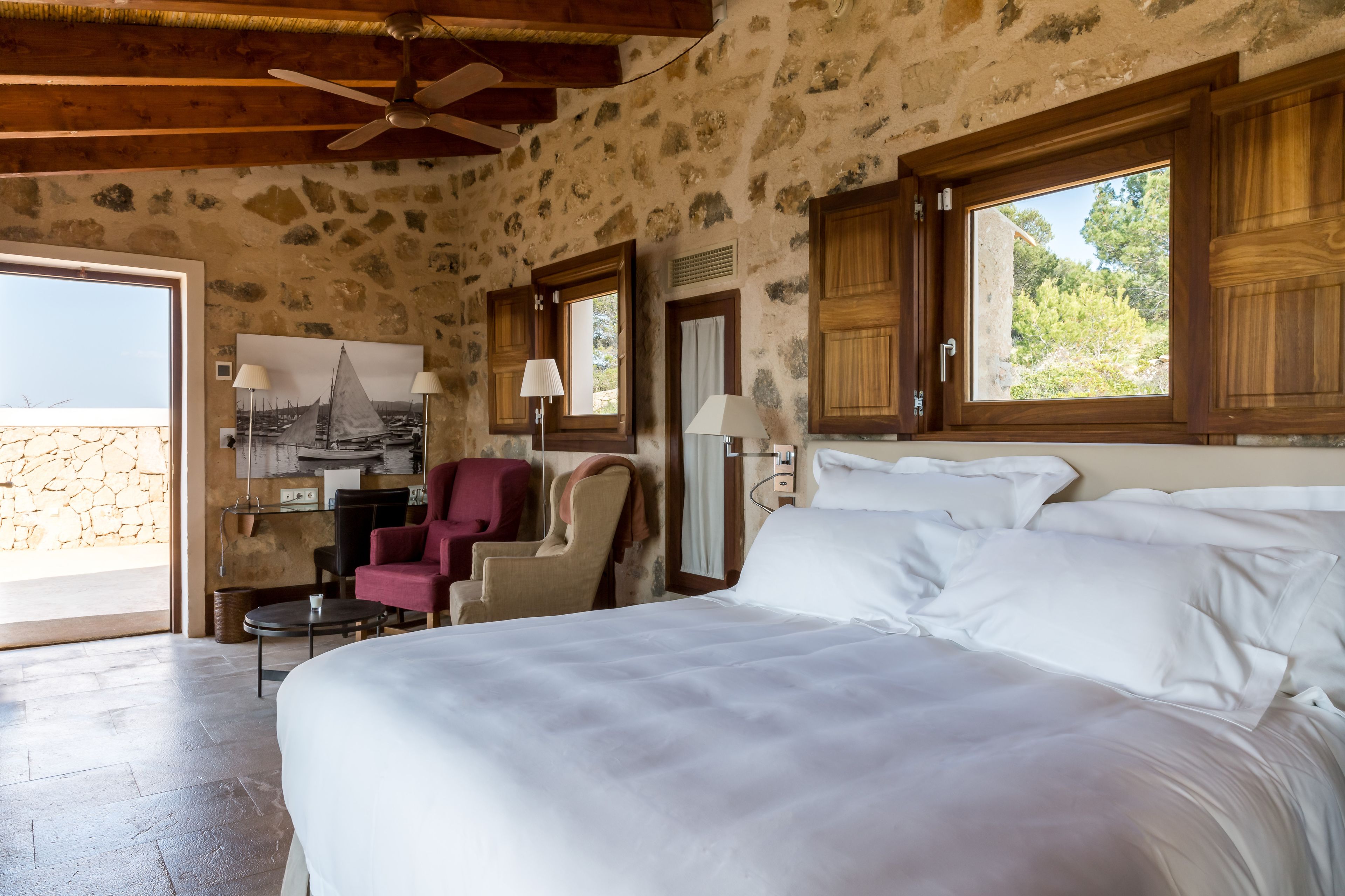 Quarto espaçoso com uma cama grande, vigas de madeira no teto, paredes de pedra e vista para o exterior.