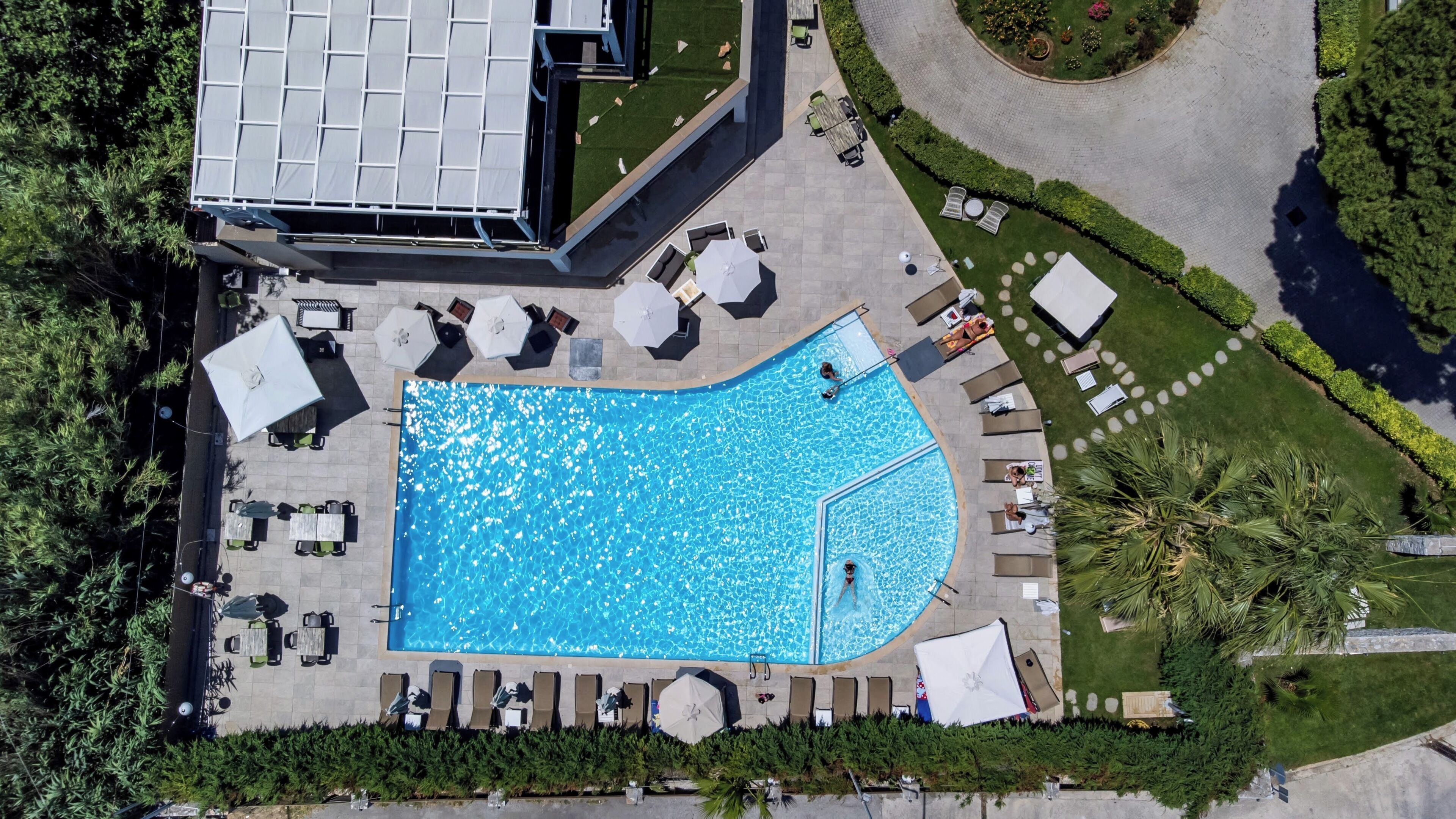Vista aérea de um hotel com piscina, espreguiçadeiras e um jardim ajardinado.