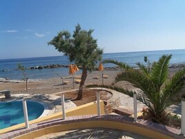 Área de piscina com vista para o mar, rodeada por palmeiras e espreguiçadeiras.