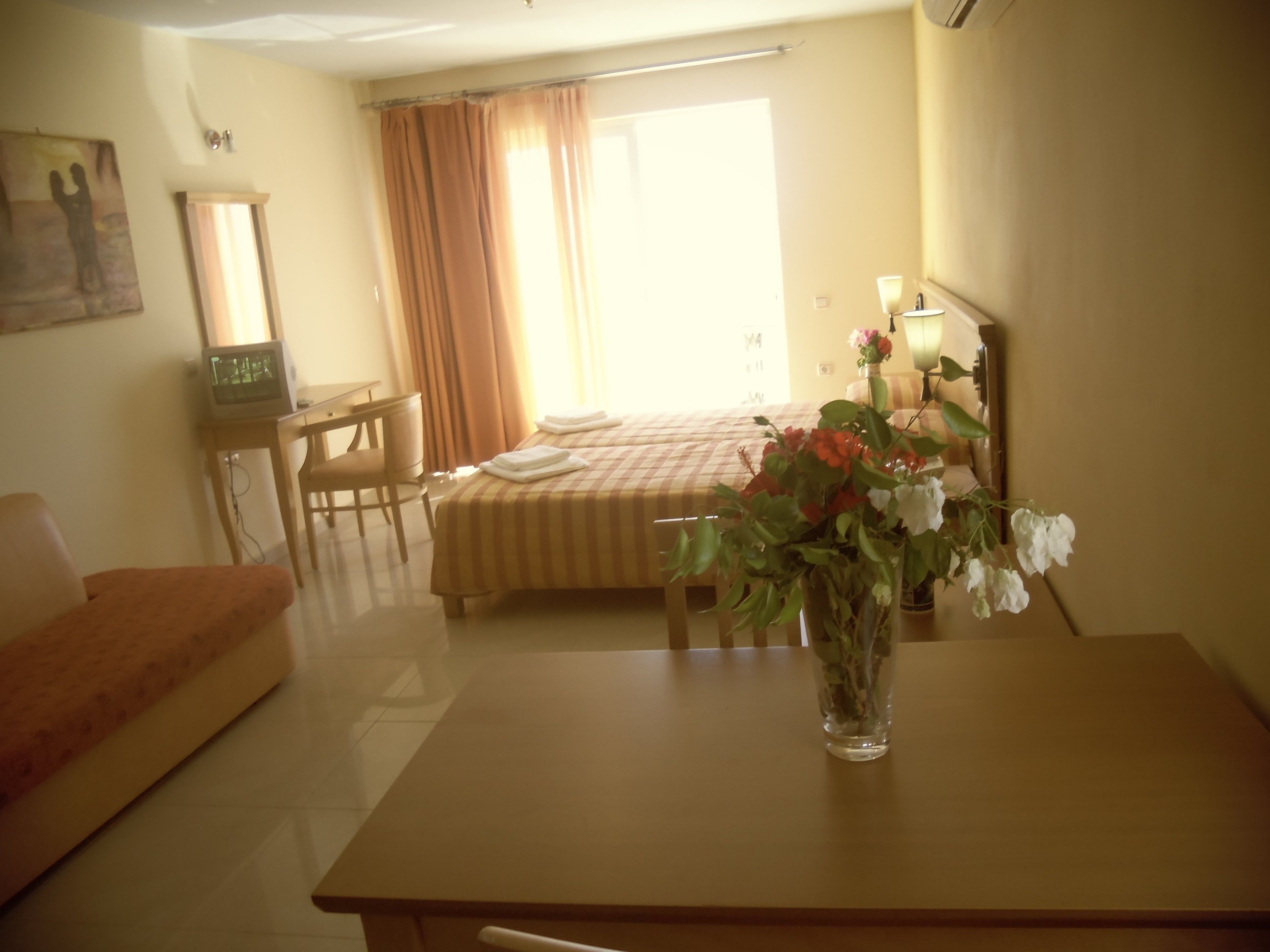 Quarto de hotel com cama, escrivaninha, cadeira, mesa e um vaso com flores.