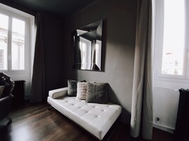 Uma sala de estar moderna com um sofá branco, um espelho grande e vista para a cidade pela janela.