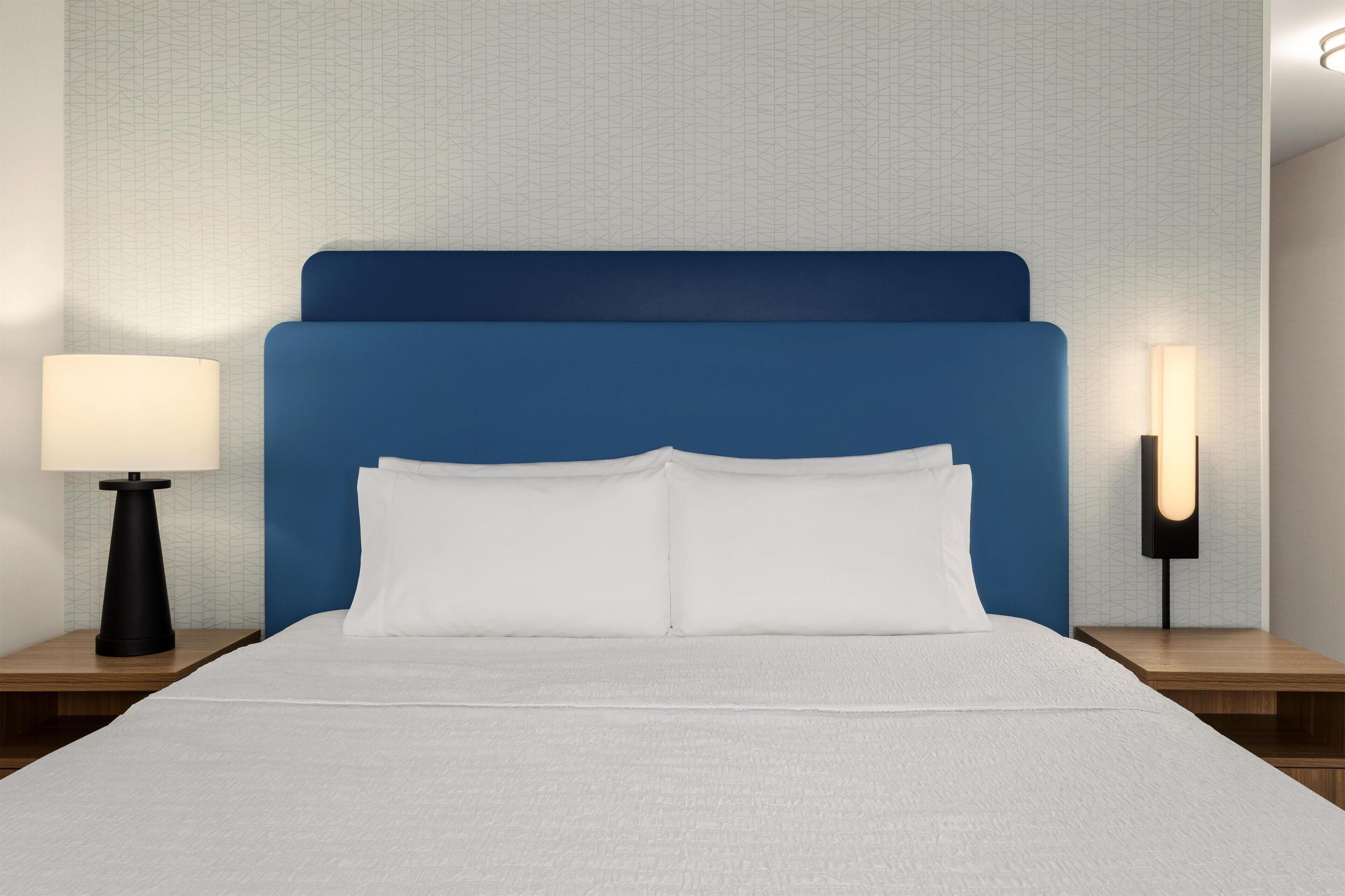 Quarto de hotel com uma cama grande, duas luminárias de cabeceira e parede com padrão geométrico.
