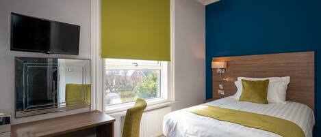 Quarto de hotel com cama, escrivaninha, cadeira, televisão e janela com vista para o exterior.