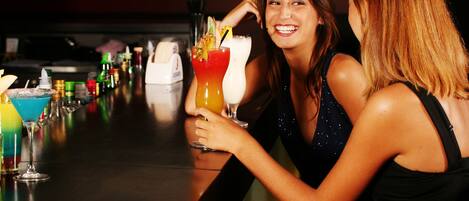 Duas mulheres sentadas em um bar com várias bebidas coloridas.