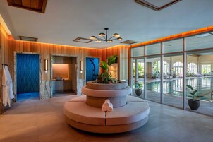 Uma área de spa com disposição circular para assentos, um balcão de recepção e uma grande janela com vista para uma piscina interna.