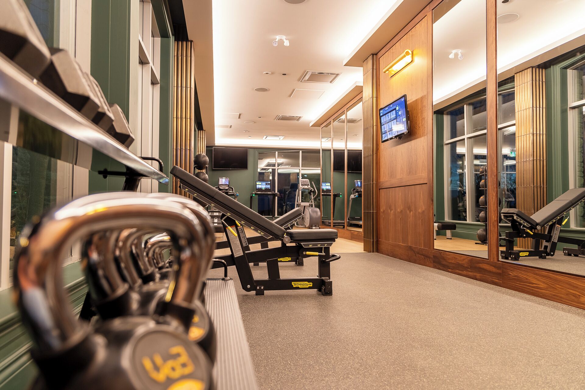 Uma academia com equipamentos de exercício, uma tela digital e um espelho.