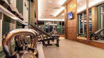 Uma academia com equipamentos de exercício, uma tela digital e um espelho.