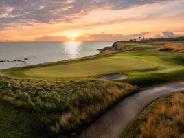 Um campo de golfe com um corpo d'água e um pôr do sol.
