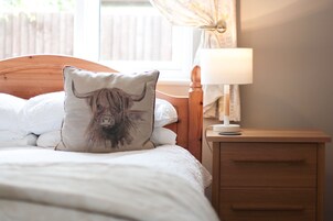 Uma cama bem arrumada, com travesseiro decorativo, luminária de cabeceira e mesa de cabeceira de madeira com gavetas.