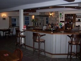 Uma área de bar com parede de pedra, balcão de madeira e vários bancos.