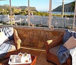 Um pátio com mobiliário de vime, uma parede de pedra e vista para o mar e colinas.