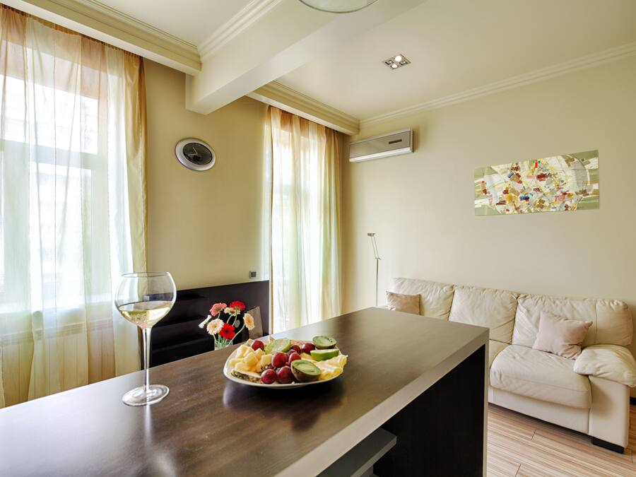 Uma área de refeições com uma mesa, um prato de frutas e um copo de vinho branco.