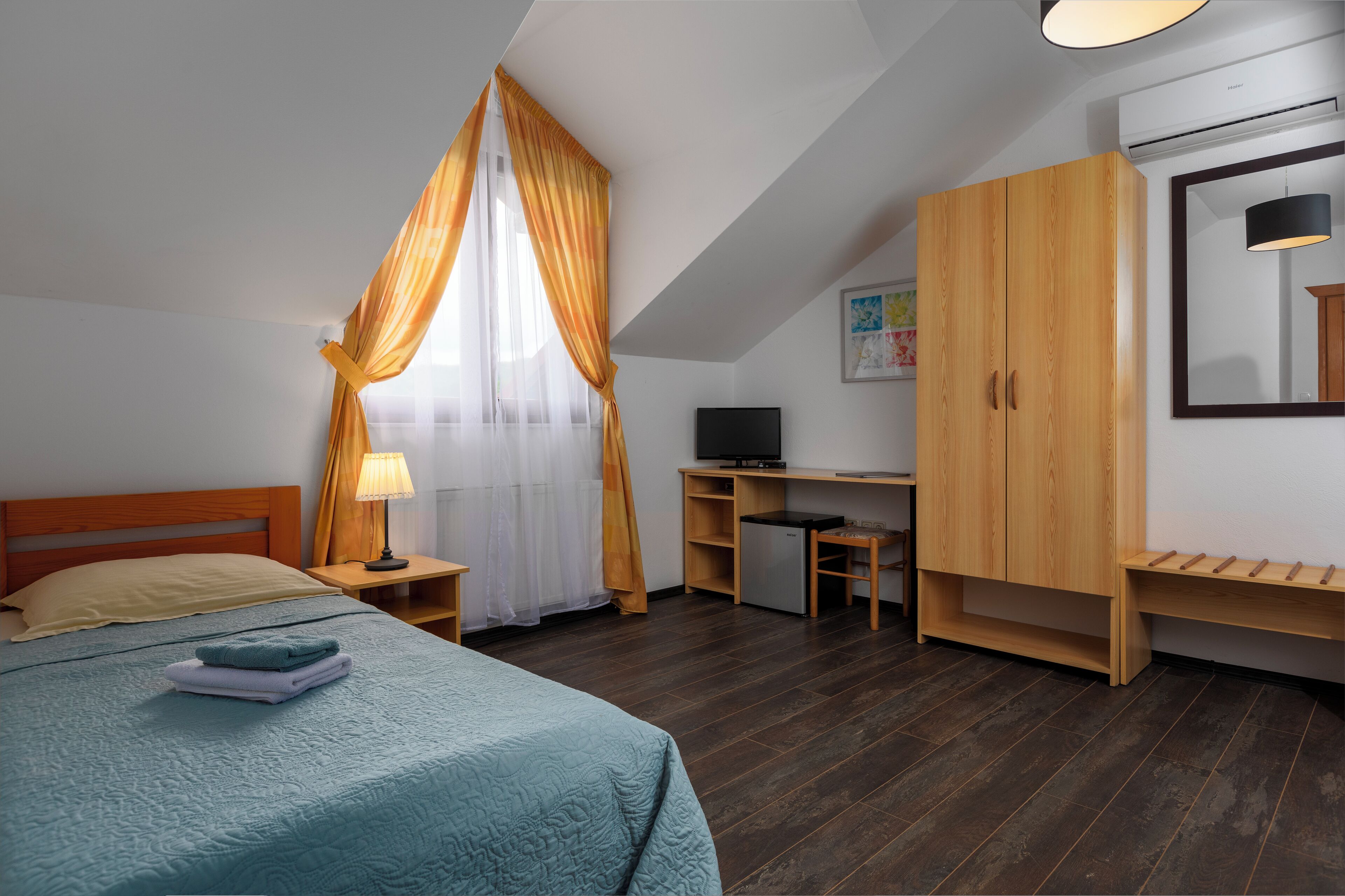 Quarto com cama, escrivaninha, televisão e guarda-roupa.