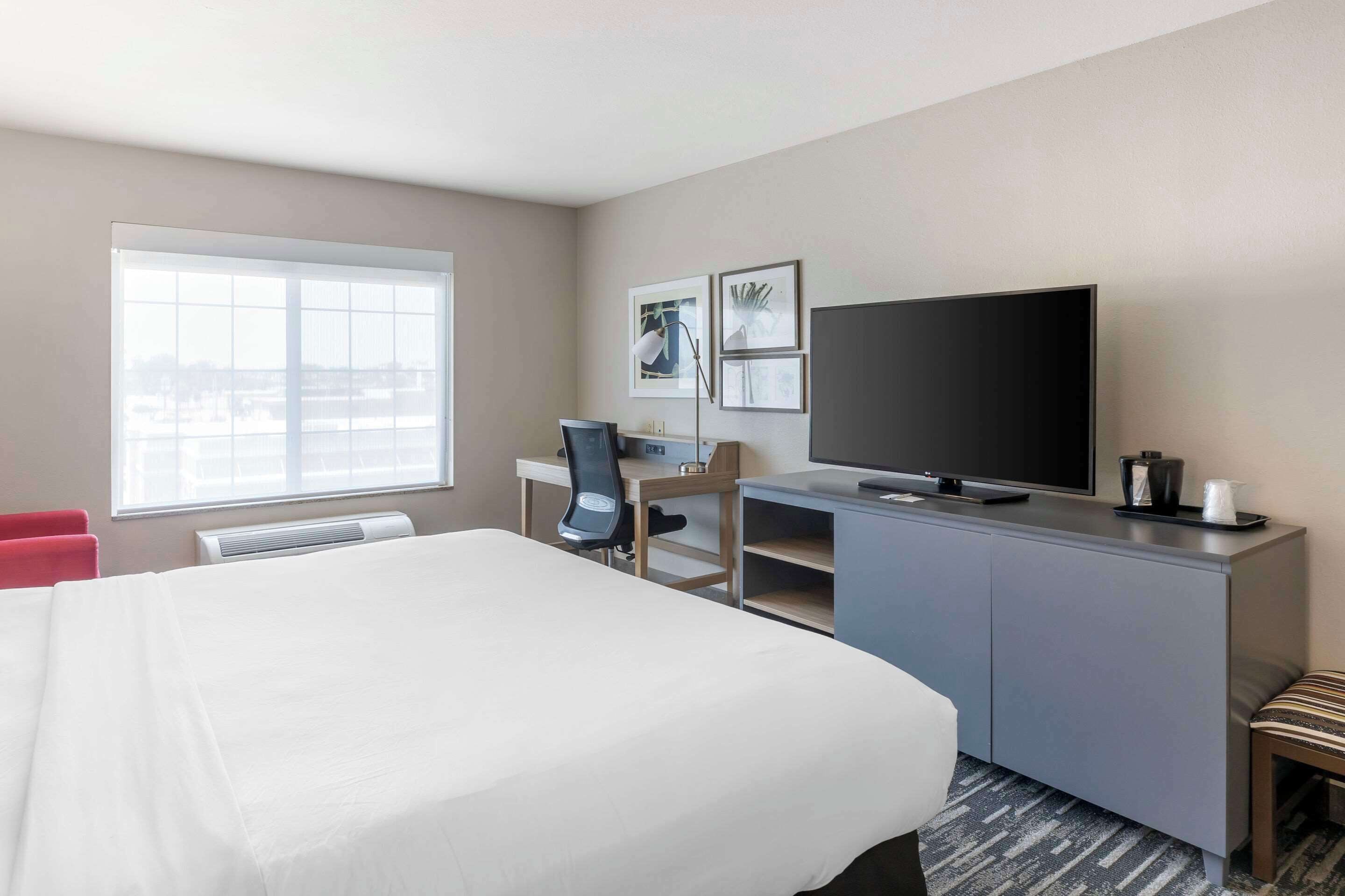 Quarto de hotel com uma cama grande, uma mesa de trabalho com cadeira, televisão e janela com vista para a cidade.
