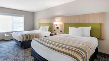 Quarto de hotel com duas camas, uma janela grande e uma luminária fixada na parede.